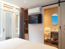 Quarto de hotel com cama, televisão fixada na parede, banheiro com pia e espelho, e ar condicionado.