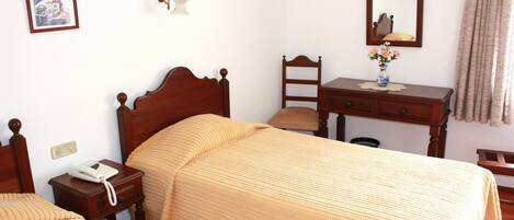 Quarto de hotel com cama de madeira, mesa de cabeceira com telefone, cômoda, cadeira, espelho e quadro na parede.