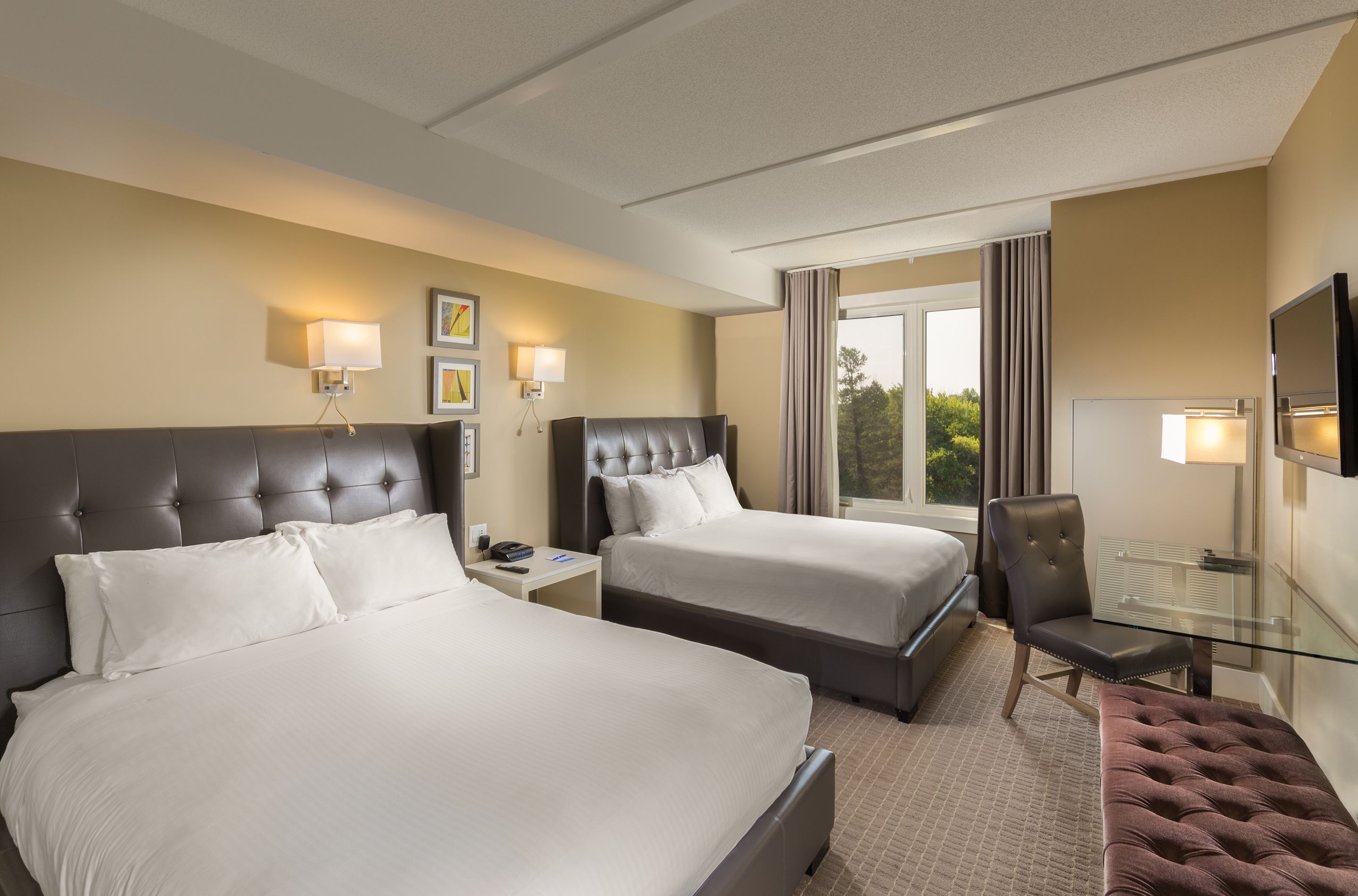 Quarto de hotel com duas camas, uma mesa de vidro, uma cadeira e uma televisão.