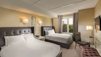 Quarto de hotel com duas camas, uma mesa de vidro, uma cadeira e uma televisão.