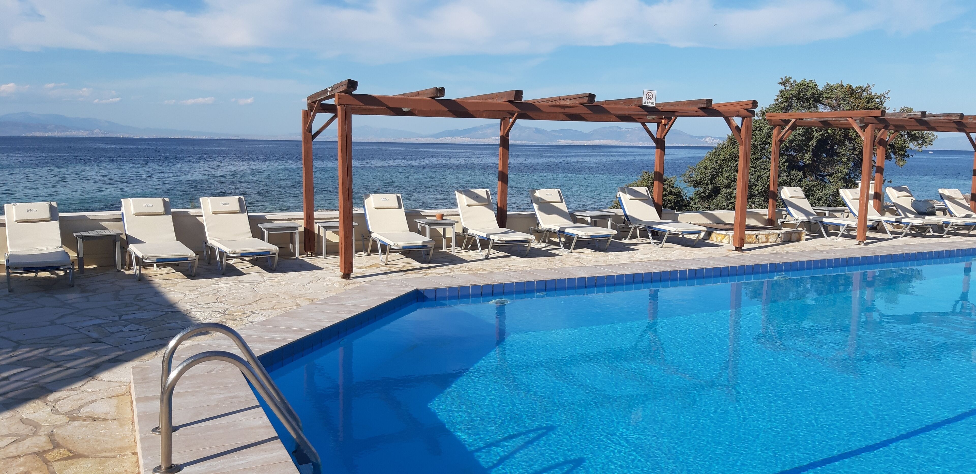 Uma área de piscina com espreguiçadeiras e um pérgola com vista para o mar.