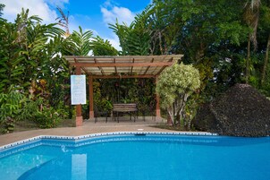 Uma área de piscina com pérgula de madeira, um banco e uma placa.