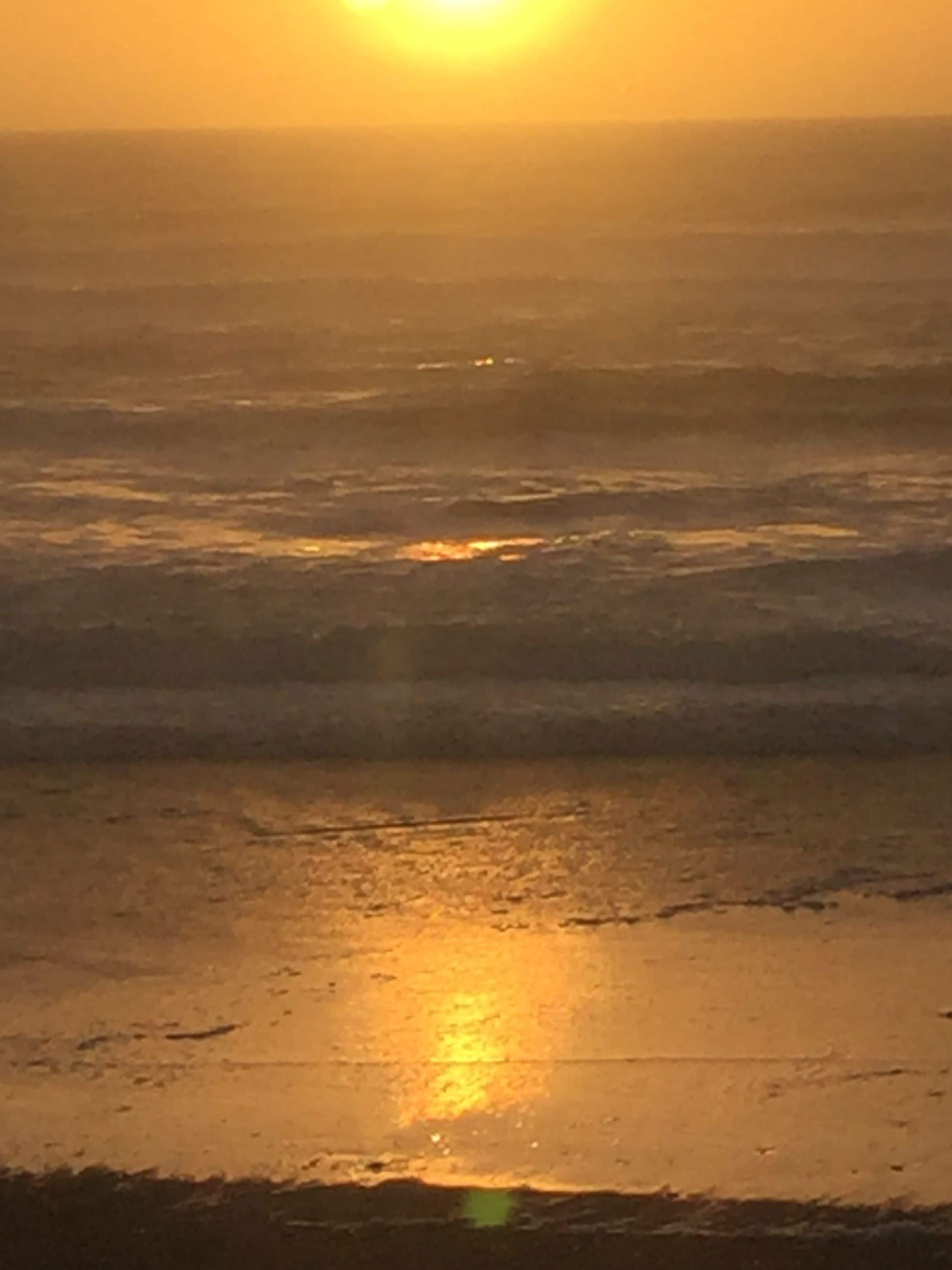 Um pôr do sol sobre o oceano, com ondas refletindo a luz do sol.