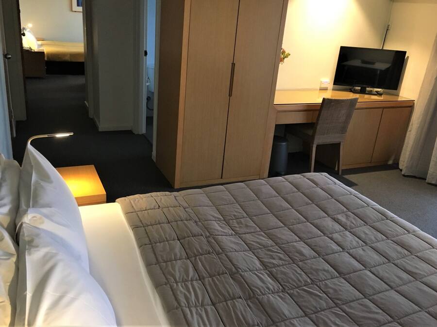 Quarto de hotel com uma cama, uma escrivaninha com cadeira, televisão e guarda-roupa.