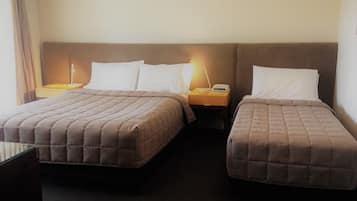 Quarto de hotel com duas camas, uma mesa de cabeceira com abajur e uma pequena mesa.