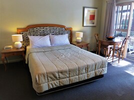 Quarto de hotel com uma cama grande, duas mesas de cabeceira com abajures, uma cadeira e uma mesinha com uma cesta de frutas.