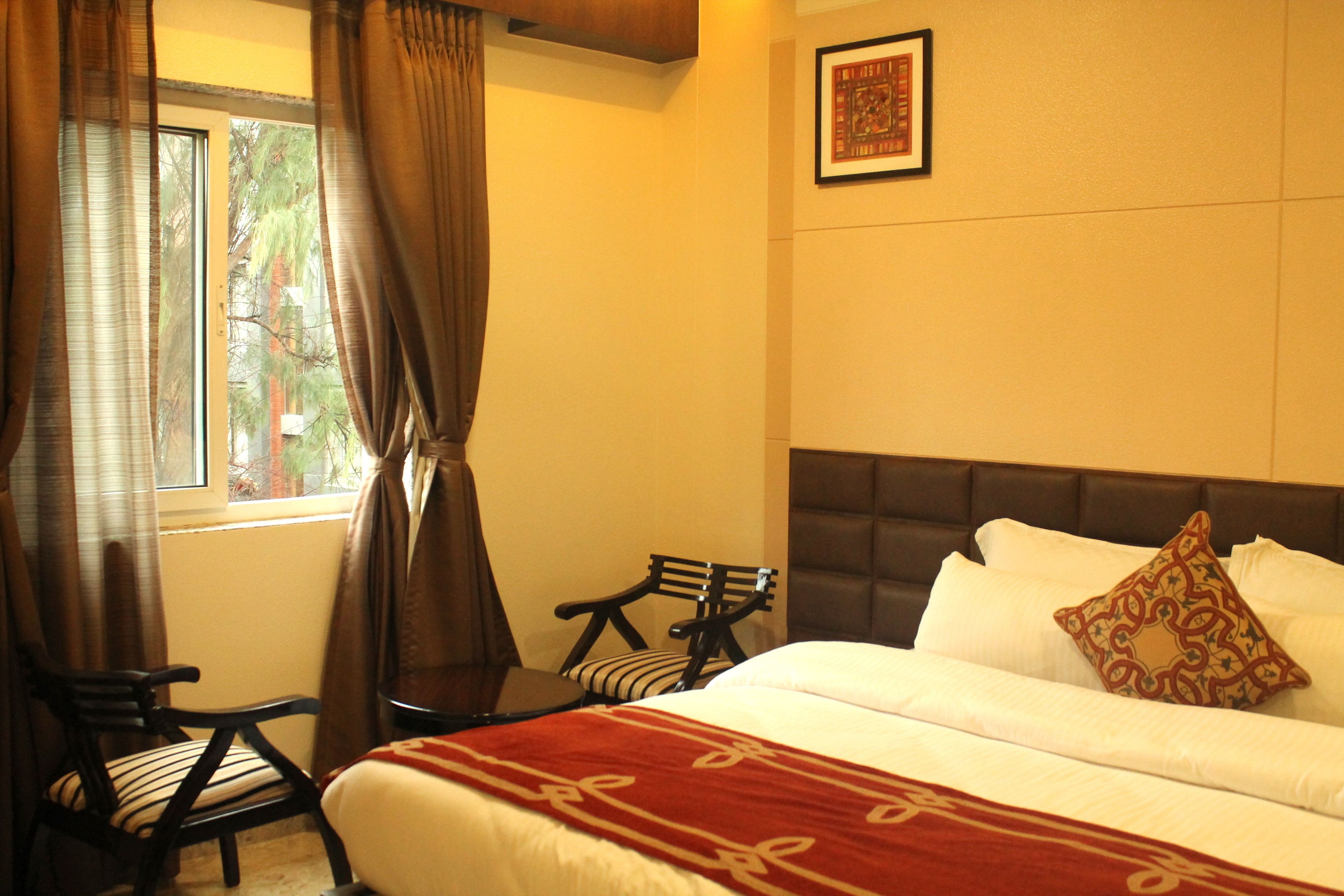 Quarto de hotel com cama, duas cadeiras, janela com cortinas e um quadro na parede.
