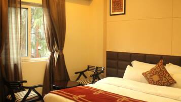 Quarto de hotel com cama, duas cadeiras, janela com cortinas e um quadro na parede.