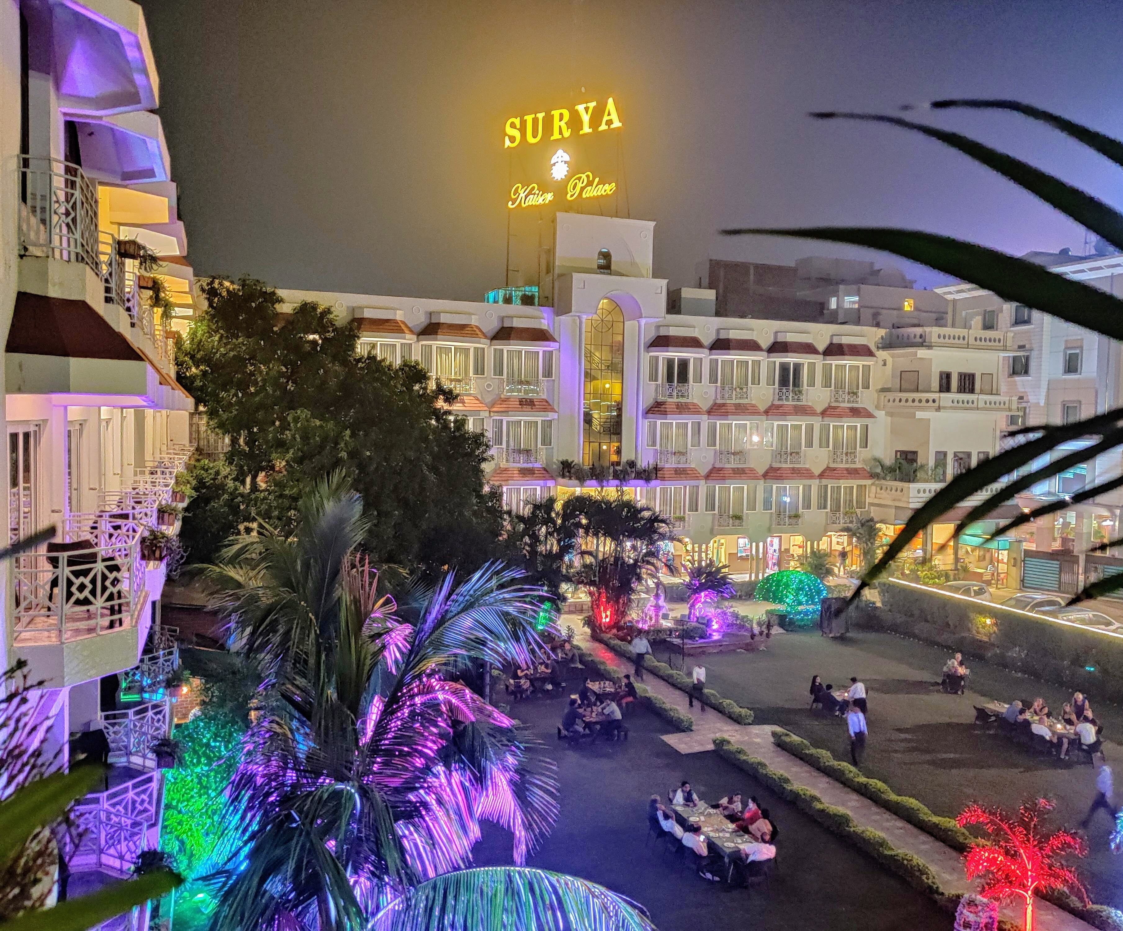 Um hotel com um letreiro chamativo 'SURYA Kaiser Palace', áreas de estar ao ar livre e caminhos bem iluminados.
