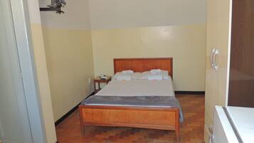 Quarto de hotel com cama de madeira, mesa de cabeceira com telefone e guarda-roupa.