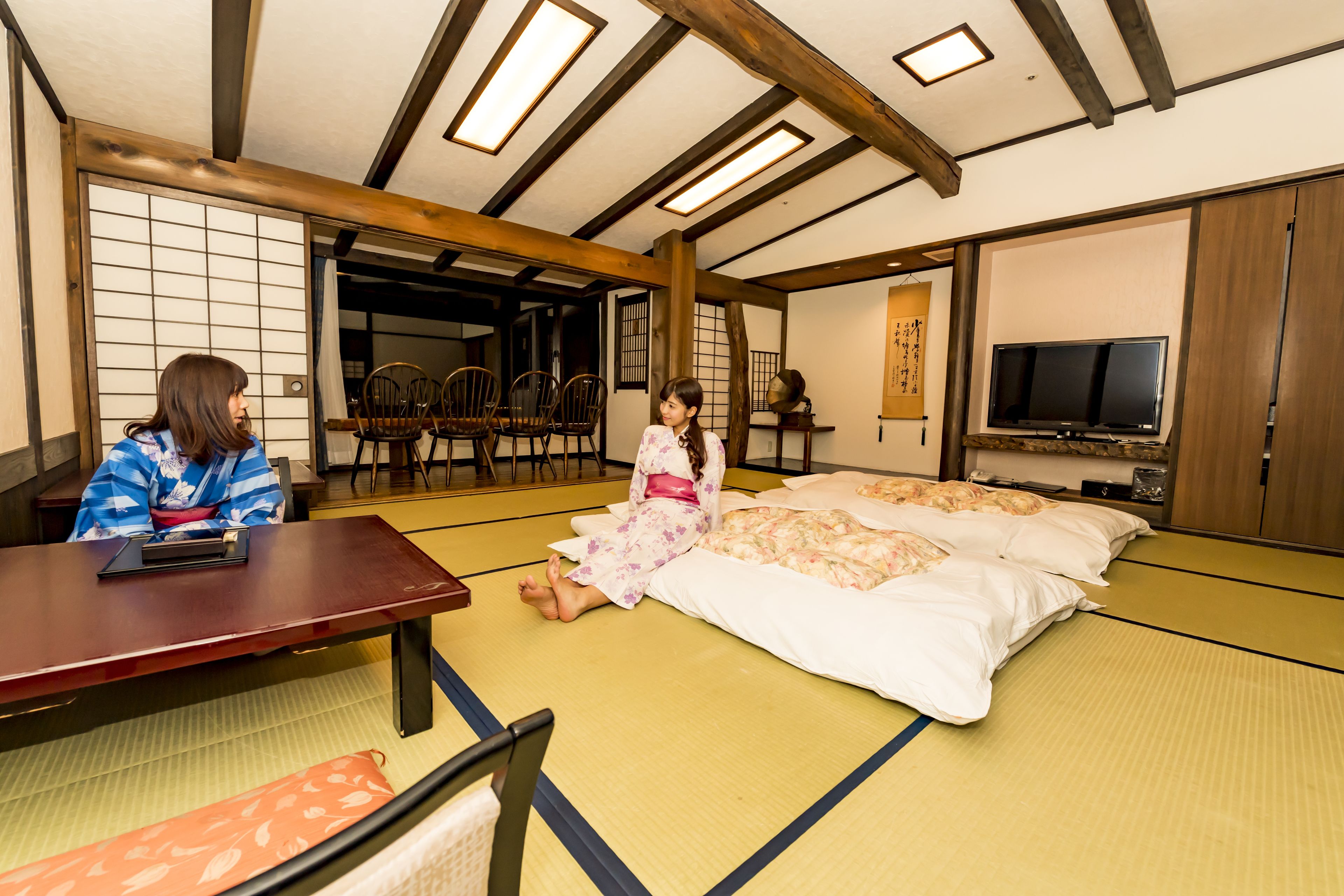 Um quarto japonês tradicional com tatames, uma mesa baixa e uma cama com almofadas.