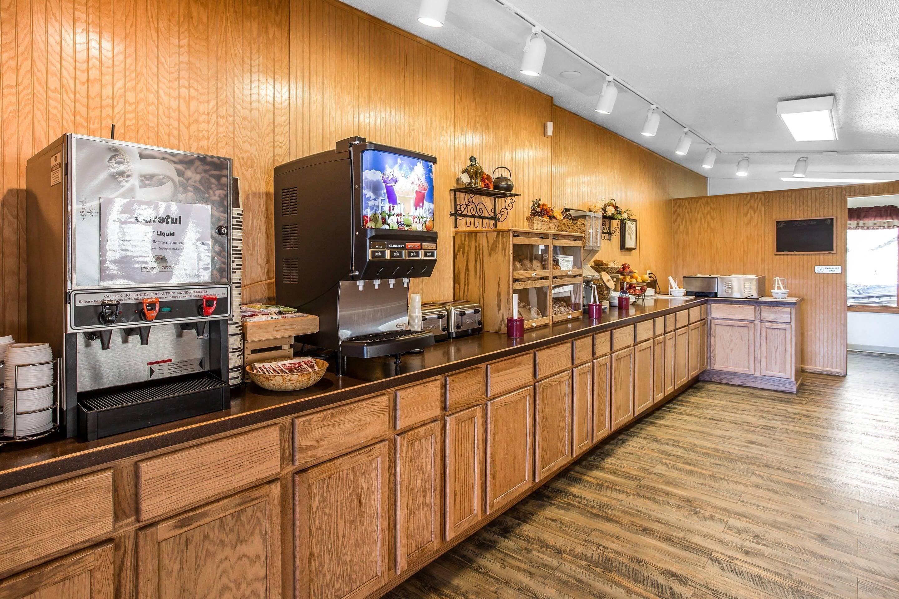 Uma estação de café por autoatendimento, com um dispensador de bebidas, uma tela de televisão e diversos alimentos no balcão.