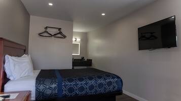 Quarto de hotel com cama, televisão, guarda-roupa e espelho.