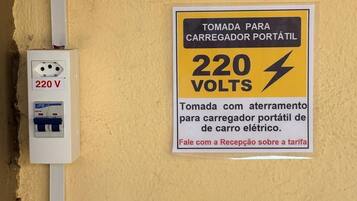 Caixa elétrica fixada na parede com uma placa indicando tomada de 220 volts para carregadores portáteis de veículos elétricos.