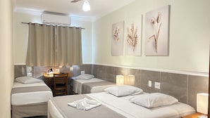 Quarto de hotel com duas camas de solteiro, uma escrivaninha com cadeira, ventoinha no teto e luminárias na parede.