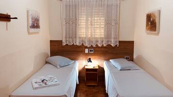 Quarto com duas camas, mesa de cabeceira com abajur e obras de arte nas paredes.