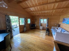 Interior de uma cabana de madeira com um sofá, uma TV e uma escrivaninha.