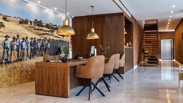 Uma área de recepção moderna com secretária de madeira, poltronas de couro e iluminação pendente.