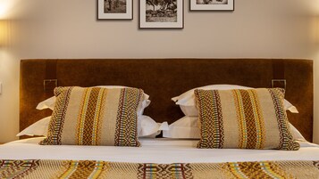 Cama com duas almofadas estampadas e um cobre-leito combinando, apoiada em uma cabeceira marrom.