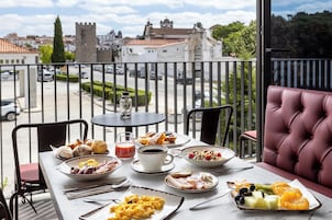 Mesa de varanda com itens de café da manhã, vista de um edifício histórico e um sofá de couro vermelho.
