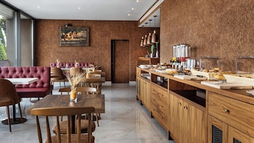 Um restaurante moderno com um sofá vermelho, mesas de madeira e um buffet com diversos alimentos.