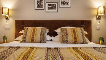 Quarto de hotel com uma cama grande, duas luminárias fixadas na parede e quadros enquadrados.