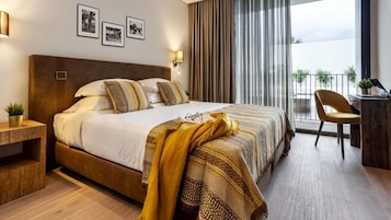 Quarto de hotel moderno com uma cama grande, uma mesa, uma cadeira e uma varanda com vista.