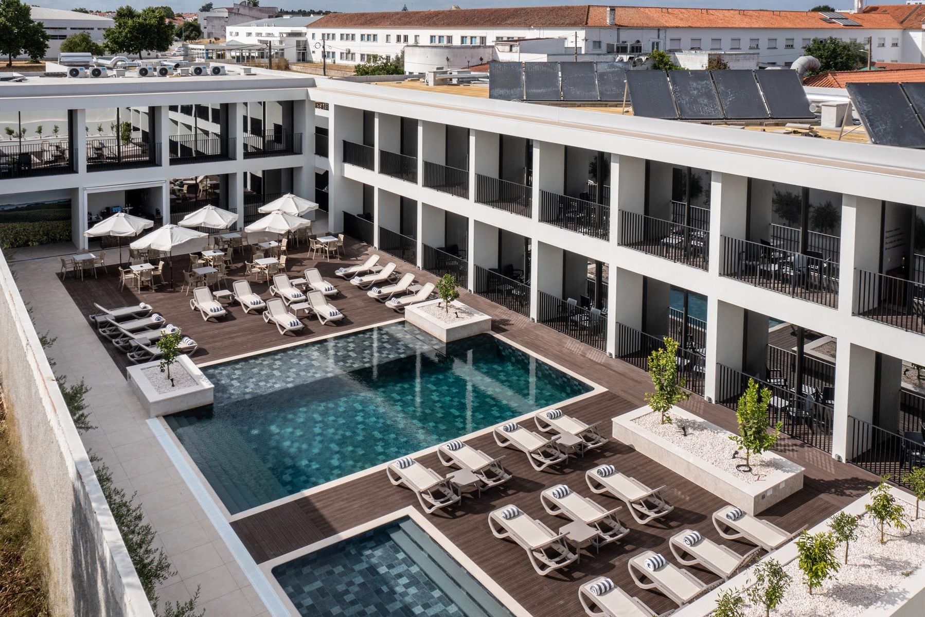 Uma área de piscina no terraço com várias espreguiçadeiras e guarda-sóis, rodeada por um edifício moderno com varandas.