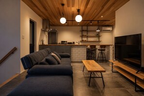 Um espaço de estar moderno com sofá, mesa de madeira, televisão e área de cozinha com balcão.