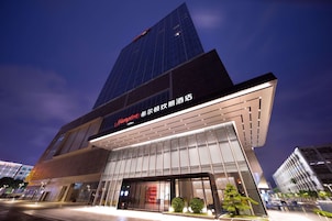Um edifício moderno de hotel com fachada de vidro destacada e sinalização com 'Hampton' e 'Hampton by Hilton'.