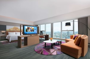 Quarto de hotel moderno com uma TV grande, um sofá, uma escrivaninha e vista para a cidade.