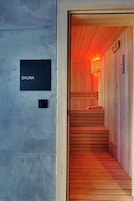 Entrada de uma sauna com interior em madeira, uma placa com a inscrição 'SAUNA' e uma parede revestida de azulejos.