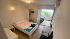Quarto com cama, mesa pequena, cadeira, guarda-roupa e varanda com vista.