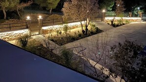 Uma área externa bem iluminada com um caminho pavimentado, paredes de pedra e árvores.