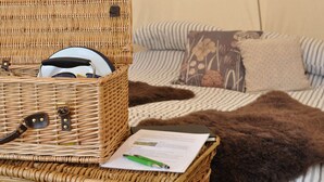 Uma cesta de vime com um laptop e uma caneta verde sobre uma cama com roupa de cama listrada e um cobertor de pele marrom.