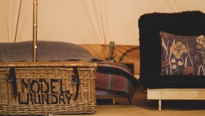 Uma cesta de vime com a inscrição 'MODEL LIVING' e uma cama com manta xadrez e almofada estampada com flores.