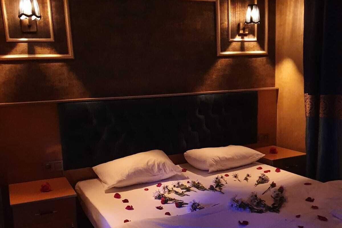 Quarto de hotel com uma cama grande, duas mesas de cabeceira e luminárias fixadas na parede.