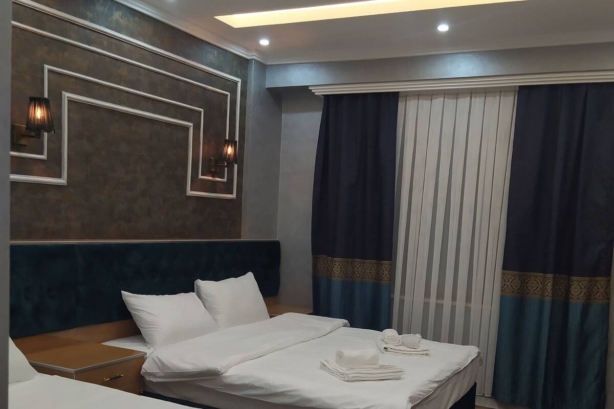 Quarto de hotel com duas camas, piso de madeira e design moderno no teto.