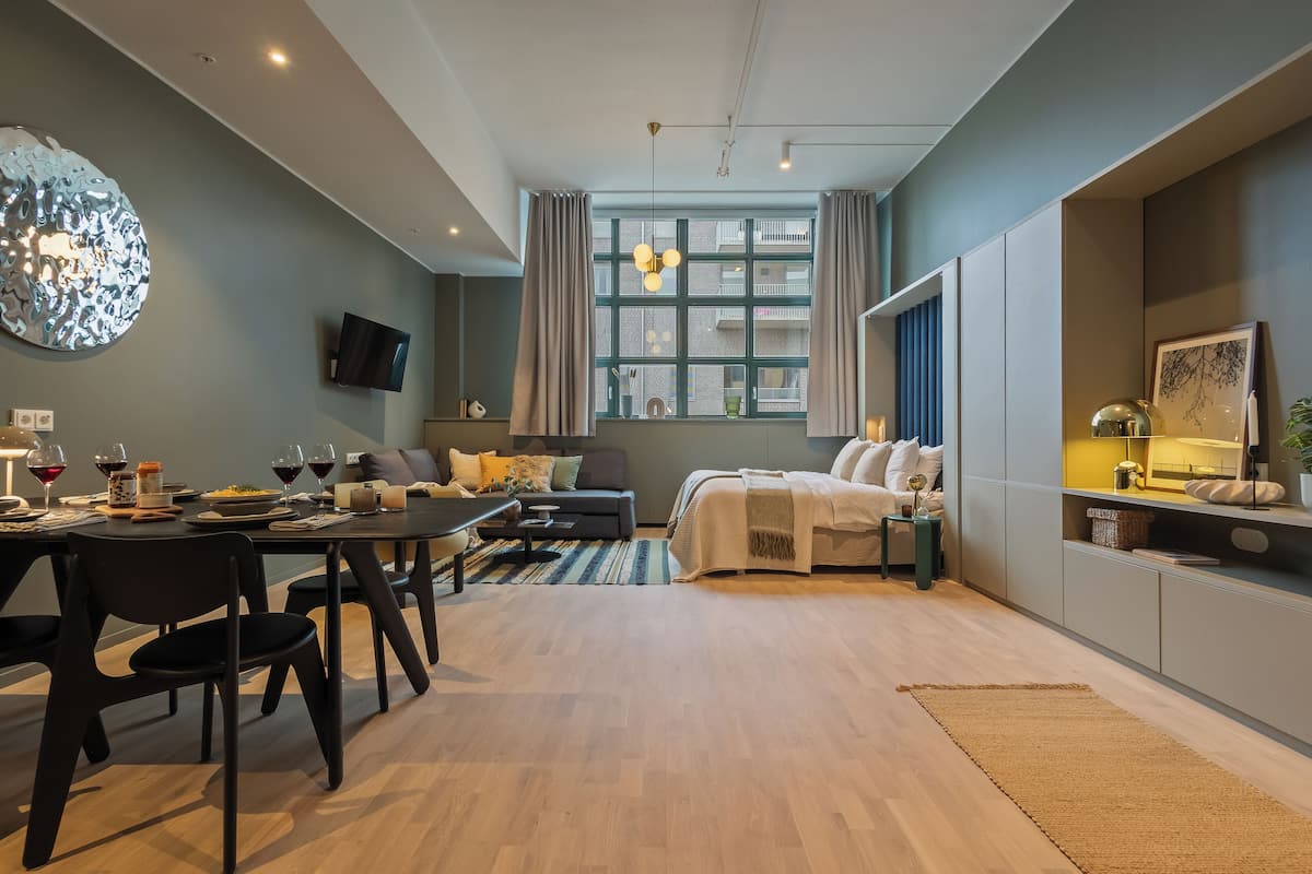 Uma sala de estar moderna com área de jantar, uma janela grande com cortinas, uma televisão de tela plana e uma cama aconchegante.