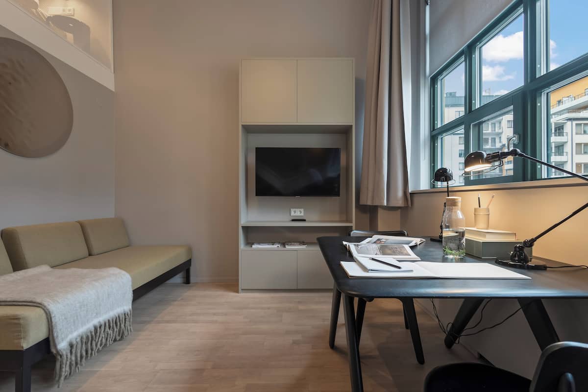 Uma sala de estar moderna com um sofá, uma mesa de jantar com um laptop, uma TV e uma janela com vista para prédios.