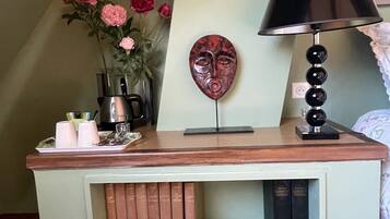 Um quarto pequeno e acolhedor com uma escrivaninha de madeira, um vaso de flores, uma máscara decorativa e um abajur.