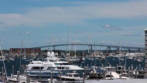 Uma marina com vários barcos atracados, uma ponte ao fundo e edifícios ao longo da orla.