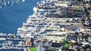 Vista aérea de uma vila costeira com um porto repleto de barcos, edifícios residenciais e uma igreja imponente.