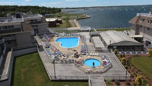 Um hotel com área de piscina, incluindo uma piscina grande e uma piscina circular menor, rodeada por espreguiçadeiras e guarda-sóis.