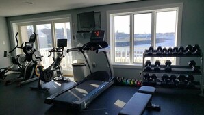 Academia com máquinas de cardio, halteres e um banco.