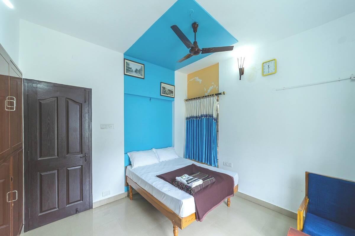 Quarto com cama, ventilador de teto, janela com cortinas e porta.
