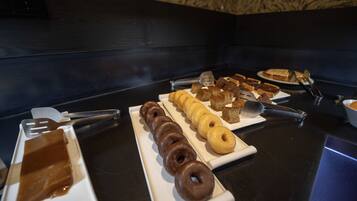 Um buffet com diversos doces e sobremesas, incluindo donuts e bolos, dispostos em pratos brancos.