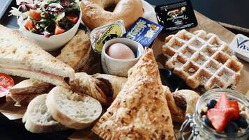 Uma bandeja com diversos itens de café da manhã, incluindo bagels, sanduíches, um waffle e uma salada.
