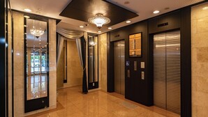 Área de elevador moderna com sinal de guia de andares, sinal de acessibilidade para cadeiras de rodas e um candelabro.