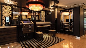 Um lobby de hotel moderno com uma mesa de recepção, um posto de autoatendimento e um grande candelabro.